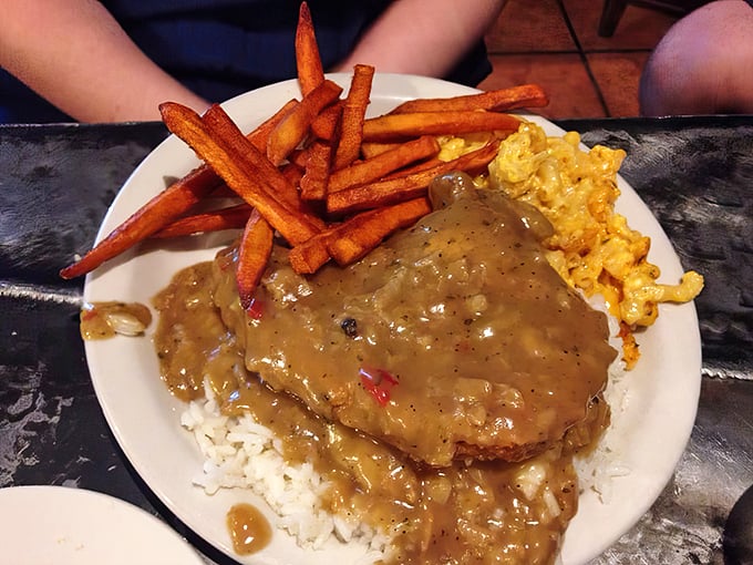 Smothered pork chop swimming in rich gravy alongside sweet potato fries and mac & cheese &ndash; a holy trinity of comfort food.