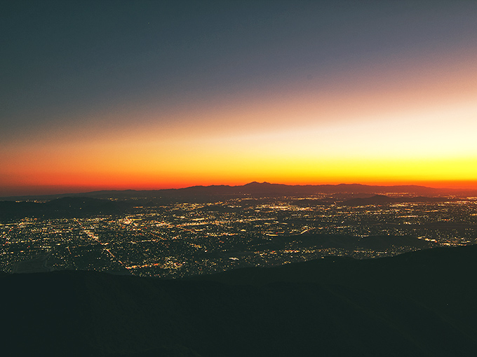 Sunset transforms the valley into a glittering metropolis. City lights below, cosmic light show above.