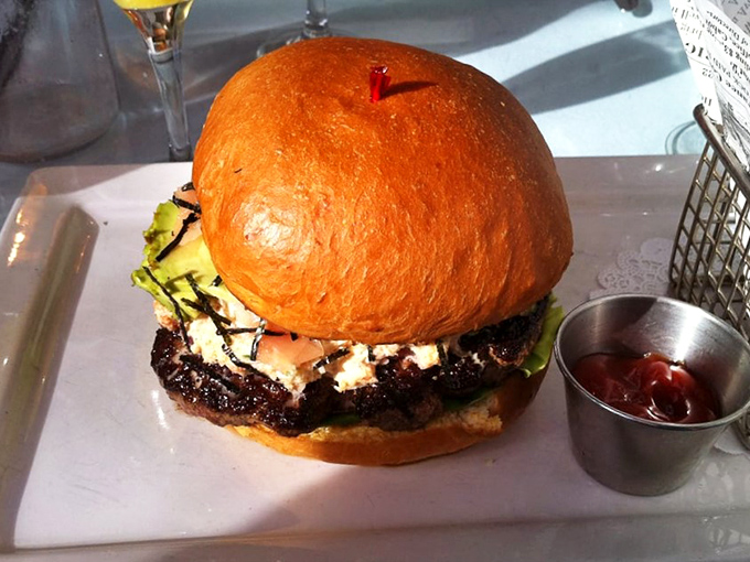 This burger defies convention with its towering presence and gourmet toppings. The small cup of ketchup seems to be saying, "You won't need me."