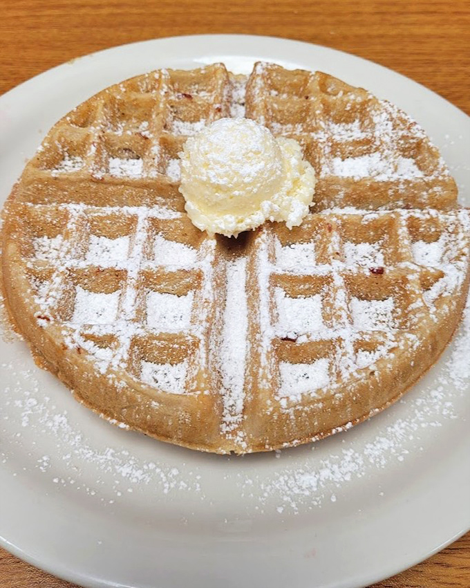 Golden waffle perfection dusted with powdered sugar. That butter crown melting slowly, creating little rivers of goodness in each square pocket.