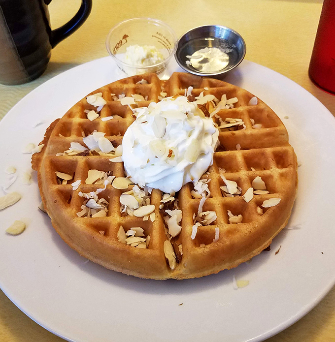 This golden waffle wears its whipped cream crown and almond confetti like royalty at a breakfast coronation.