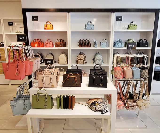 A rainbow of handbags arranged with museum-quality precision, proving that organization can be deeply, wonderfully satisfying to witness.