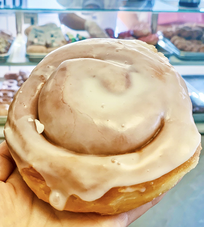 The cinnamon roll glistens with sweet glaze, promising the kind of comfort that makes Monday mornings slightly less offensive to humanity.