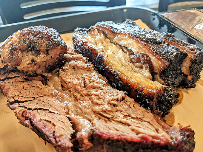 The holy trinity of barbecue: pork belly, brisket, and ribs sharing a plate like old friends at a high school reunion.