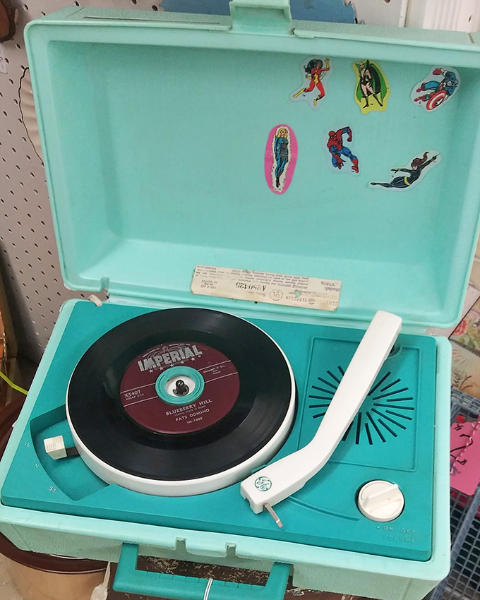 A turquoise record player adorned with superhero stickers&mdash;childhood dreams and teenage anthems preserved in portable plastic perfection.