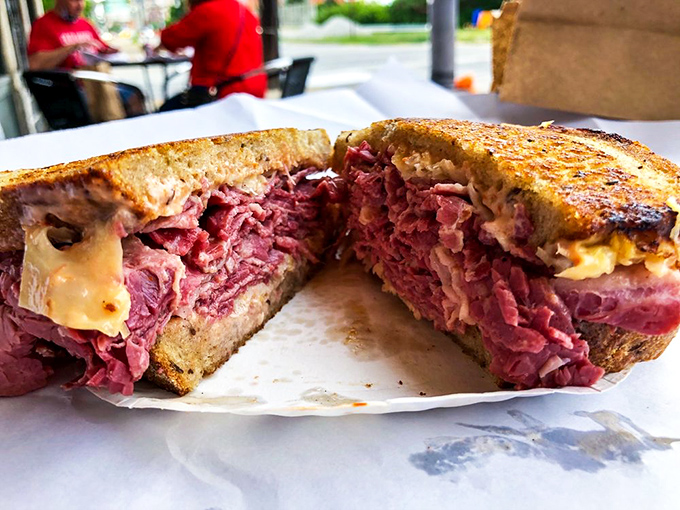 The Reuben cross-section reveals layers of corned beef glory, melted cheese, and sauerkraut in perfect architectural harmony together.