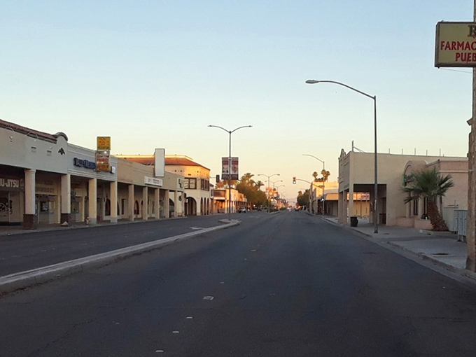 Twilight paints Brawley's wide boulevard in honey hues, transforming humble stucco into Spanish colonial elegance as streetlights flicker to life.