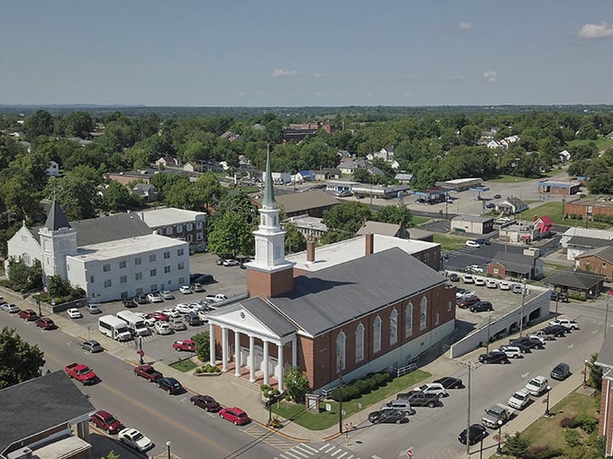Steeple skyline symphony! From above, Harrodsburg's impressive brick church with its gleaming white columns and soaring steeple anchors a neighborhood that looks like Mr. Rogers designed it himself.