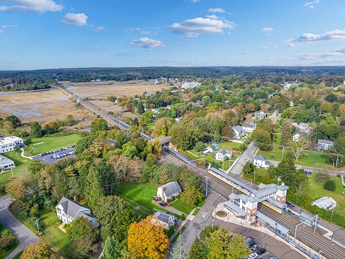 A breathtaking aerial view of Madison, Connecticut, where historic homes nestle among autumn trees near the train station and shoreline.