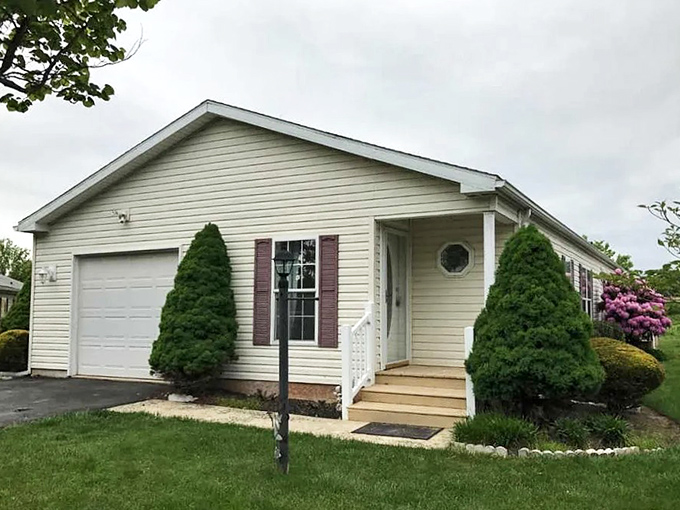 Single-story living with burgundy shutters and twin evergreen sentinels—like a retirement welcome committee that never asks awkward personal questions.