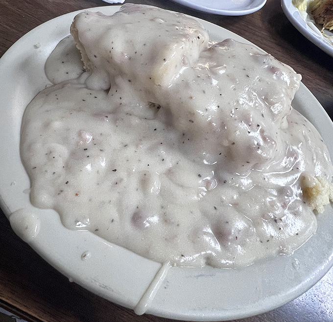 Biscuits and gravy so generous they've completely surrendered to their creamy, peppery fate—fork required, no judgment if you lick the plate.