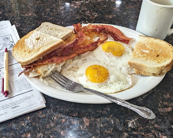 The breakfast trinity: perfectly fried eggs, crispy bacon, and hash browns that crackle with each forkful&mdash;morning salvation on a white plate.