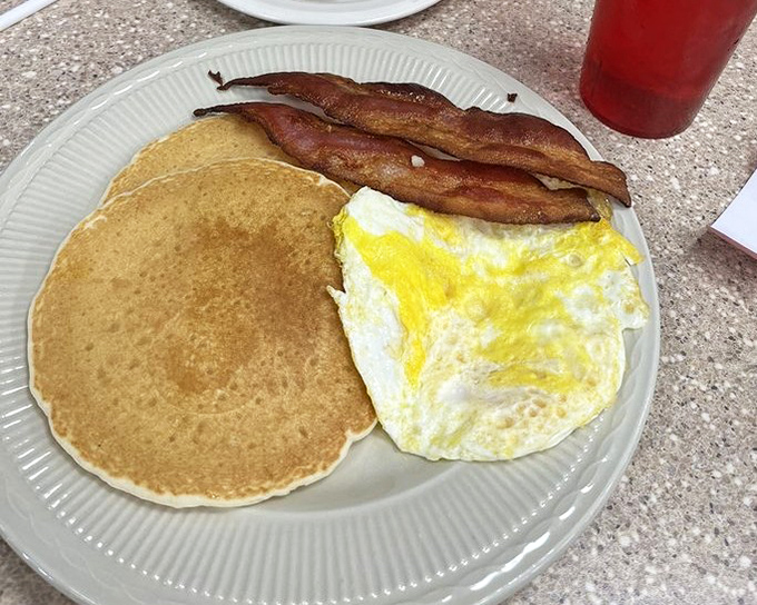 The holy trinity of breakfast: golden pancake, perfectly fried egg, and bacon that strikes the ideal balance between crisp and chewy. Simple perfection on a plate.