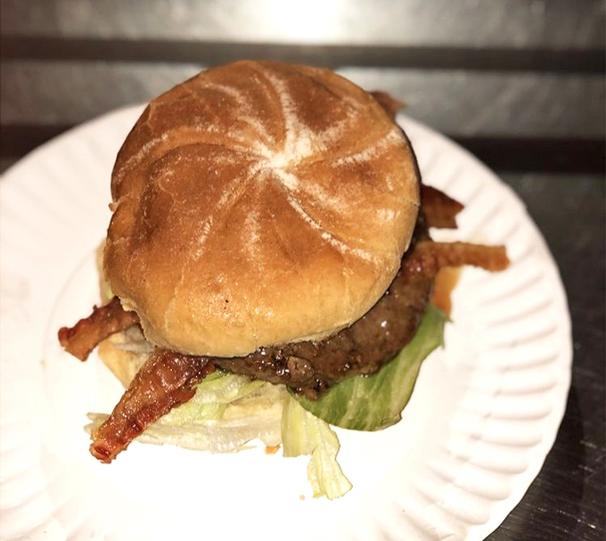 The burger arrives on its paper throne, bacon standing at attention like crispy sentinels guarding the juicy patty beneath a perfectly toasted crown.