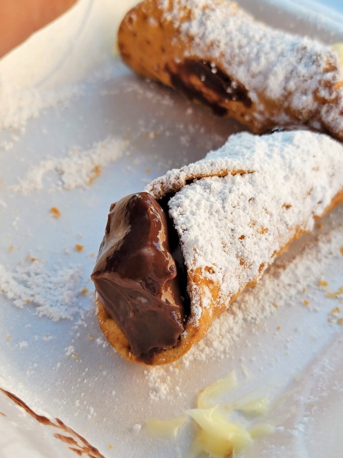 Fresh cannolis dusted with powdered sugar like edible snow globes filled with sweet ricotta dreams and chocolate chips inside.