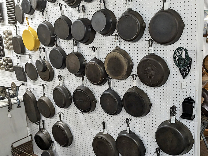 Cast iron cookware wall&mdash;where modern non-stick pans come to feel inadequate. That single yellow pan among the black is like finding Waldo in a sea of perfectly seasoned history. 