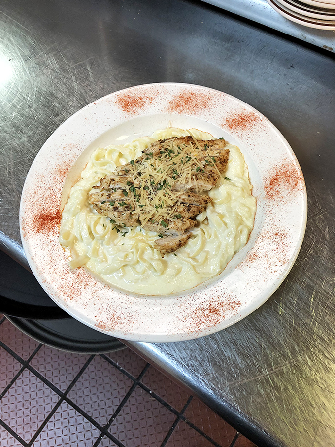 Comfort food elevated: tender chicken over creamy pasta, dusted with herbs and parmesan. The plate's paprika rim isn't just decoration&mdash;it's a promise of flavor.