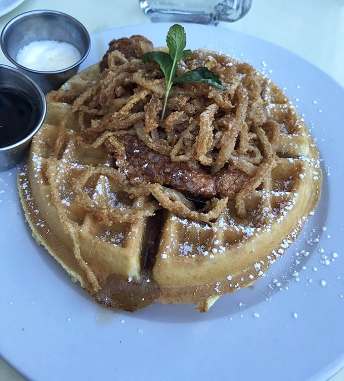 Chicken and waffles with a crown of crispy onions. The maple syrup stands ready to create that sweet-savory magic that makes taste buds dance.