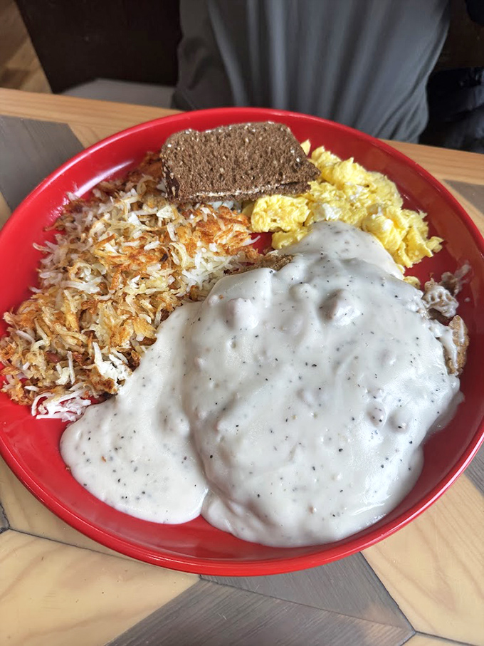 A red bowl symphony of crispy potatoes, fluffy eggs, and gravy that could convert even the most dedicated lunch enthusiast.