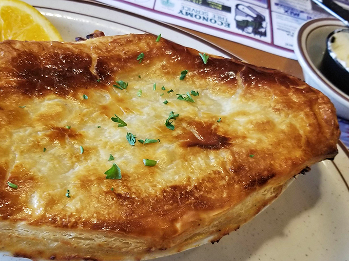 Golden, flaky crust hiding a steaming chicken pot pie interior&mdash;comfort food architecture at its finest, with fresh herbs adding a touch of color.