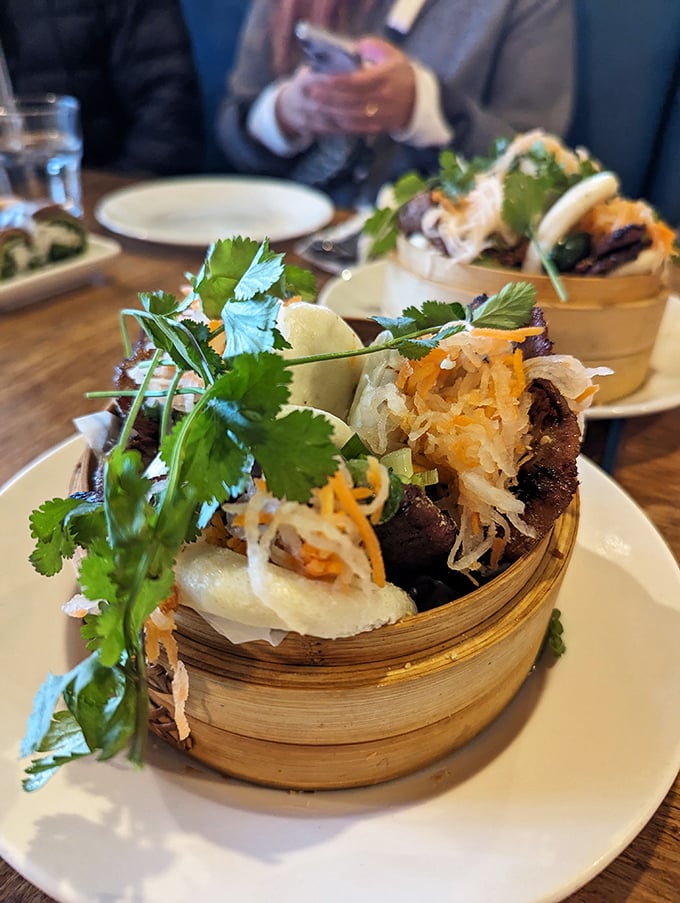 Bamboo steamer, flavor bomb! These bao buns arrive garnished with fresh cilantro and shredded vegetables, creating the perfect handheld delight for your culinary adventure.