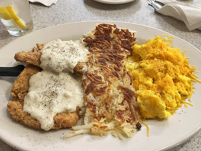 The holy trinity of diner perfection: chicken fried steak smothered in gravy, crispy hashbrowns, and scrambled eggs that look like morning sunshine on a plate.