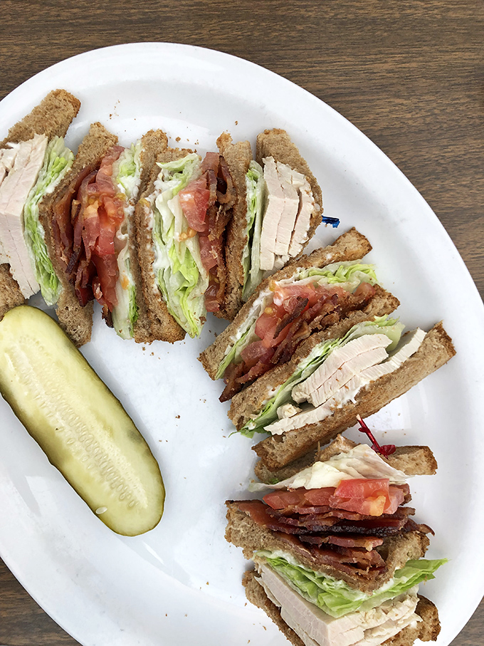 The club sandwich: architectural marvel of turkey, bacon, and lettuce. Skyscrapers of flavor requiring strategic structural planning to eat.