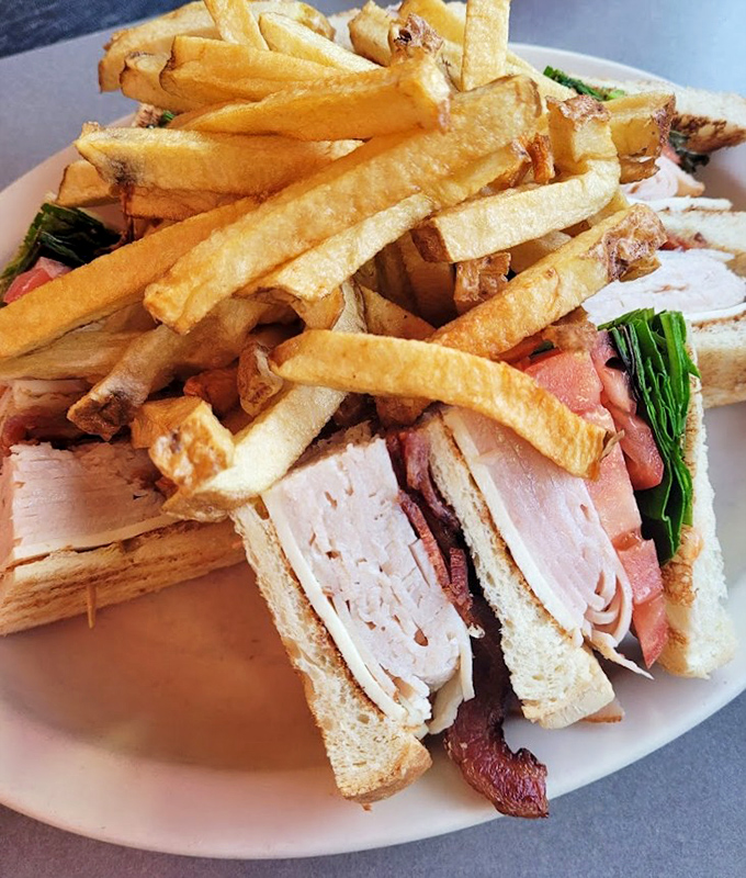A club sandwich that requires jaw exercises before attempting, with fries standing at attention like crispy golden soldiers.