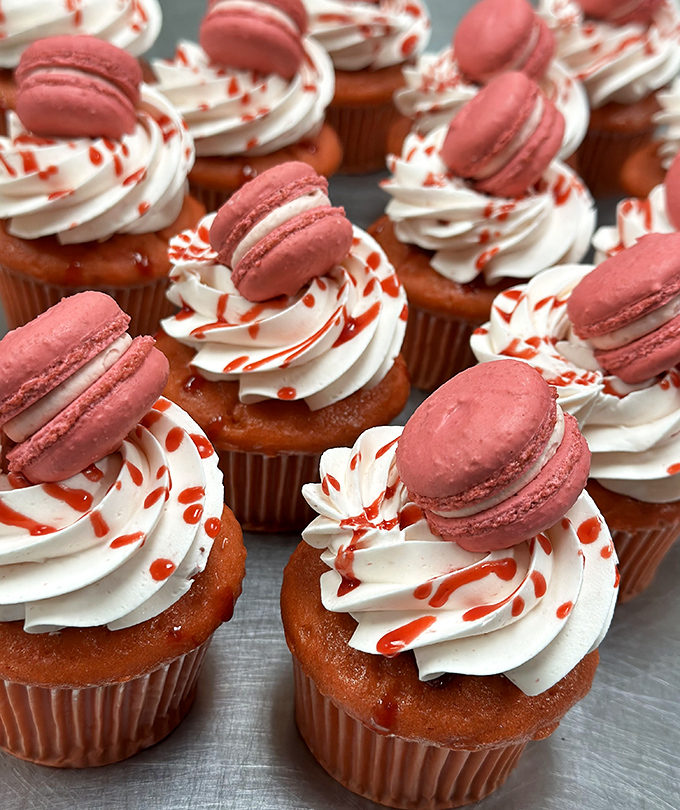 Cupcakes wearing tiny pink macaron hats &ndash; because even desserts deserve fashion accessories. Whimsical treats that taste as good as they look.