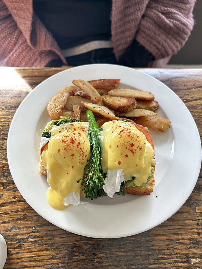 Eggs Benedict reimagined with vibrant greens and country potatoes that make you question why anyone bothers with basic breakfast when this exists.
