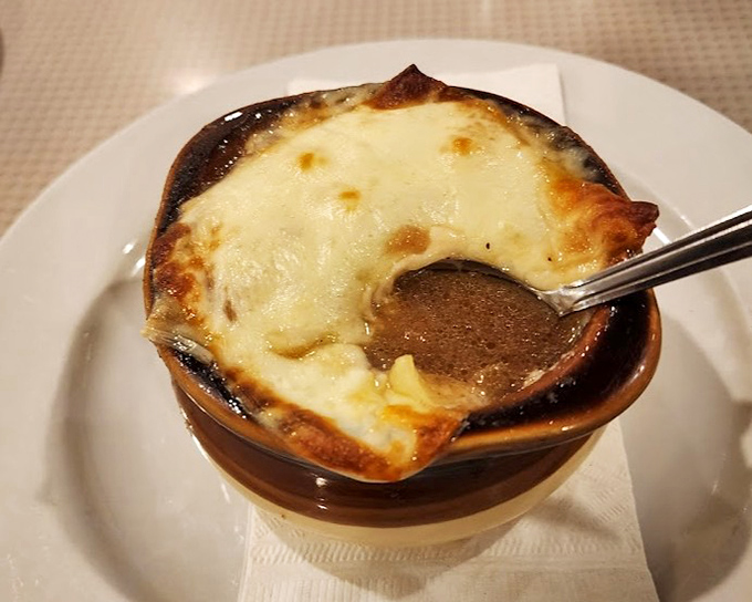 French onion soup with a cheese cap so perfect it deserves its own superhero cape. The spoon breaking that crust is food theater at its finest.