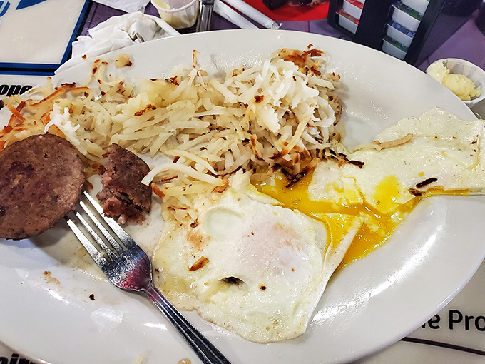 A classic American breakfast plate where the sunny-side-up egg yolk creates nature's perfect sauce for crispy hash browns and savory sausage patties.
