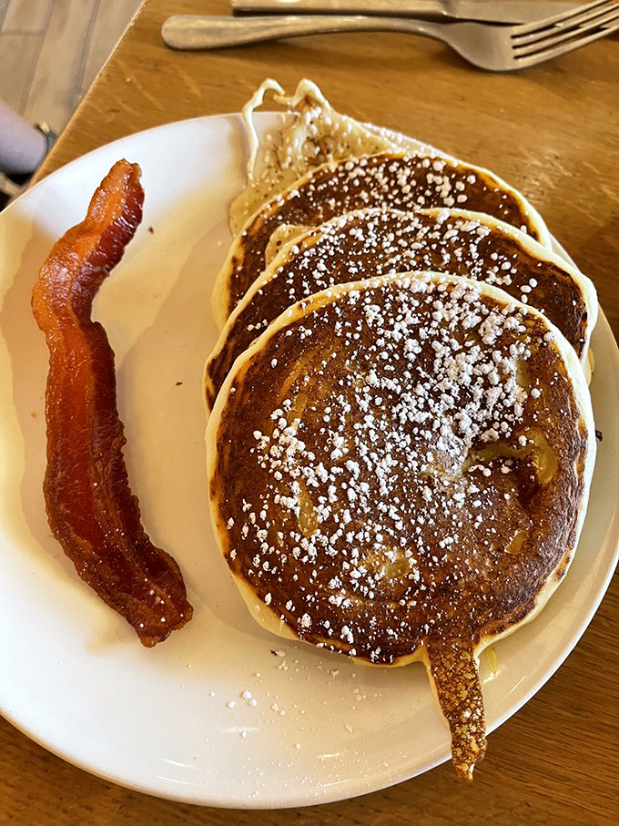 Golden-brown pancakes dusted with powdered sugar alongside crispy bacon &ndash; breakfast's perfect power couple that never disappoints.
