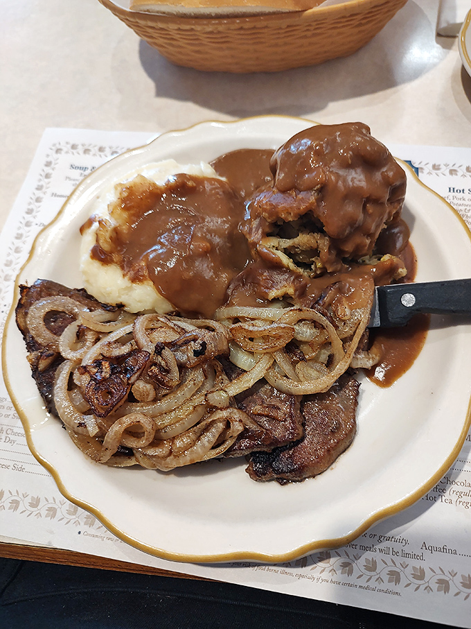 A carnivore's dream plate: perfectly seared steak smothered in caramelized onions alongside mashed potatoes drowning happily in rich brown gravy.