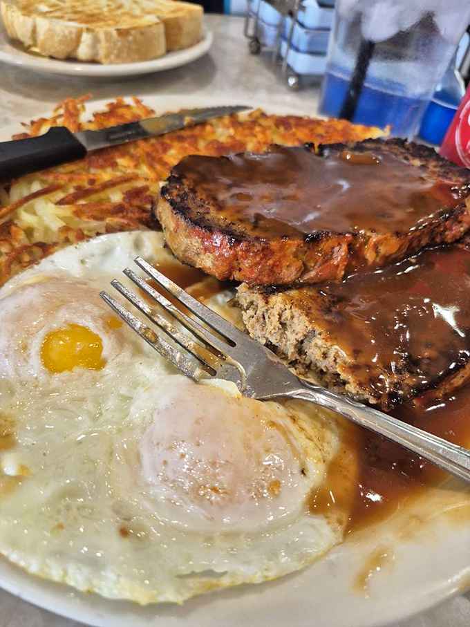 The breakfast of champions: eggs sunny-side up, crispy hash browns, and meatloaf smothered in gravy &ndash; a plate that says "go back to bed" and "conquer the world" simultaneously.