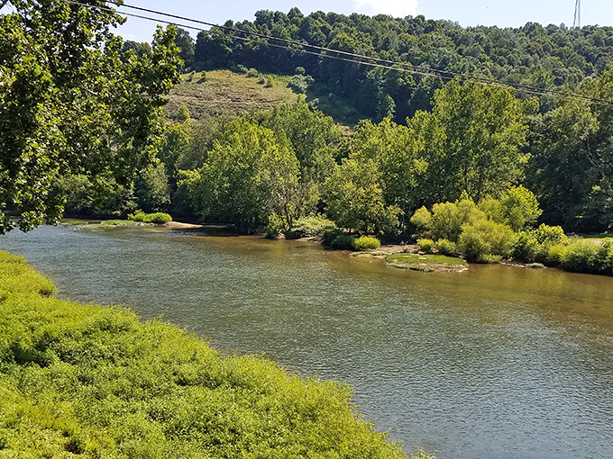 The Tygart Valley River flows peacefully beneath the bridge, its gentle current carrying centuries of stories past those sturdy stone pillars.