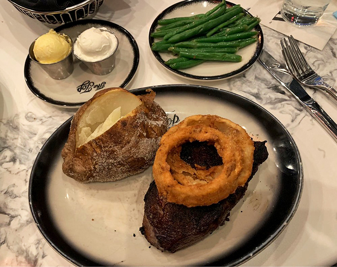 A steak with an onion ring crown&mdash;because even royalty needs the perfect accessory. The baked potato stands ready for its supporting role.