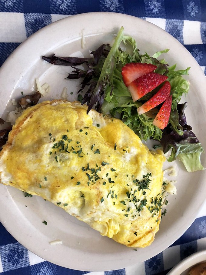 An omelet that clearly went to finishing school. Perfectly folded, herb-flecked, and accompanied by fresh greens and strawberries for that touch of color.