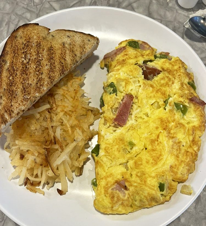 An omelet that actually contains visible ingredients rather than hiding them like state secrets. Paired with hash browns that clearly graduated with honors.