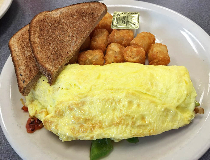 This omelet doesn't just contain ingredients; it embraces them in a fluffy egg hug, while those golden tater tots stand ready for their supporting role.