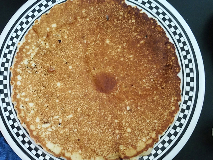 This pancake spans nearly plate-to-plate, a golden-brown canvas ready for the sweet embrace of butter and maple syrup—breakfast of champions and night-shift workers alike.