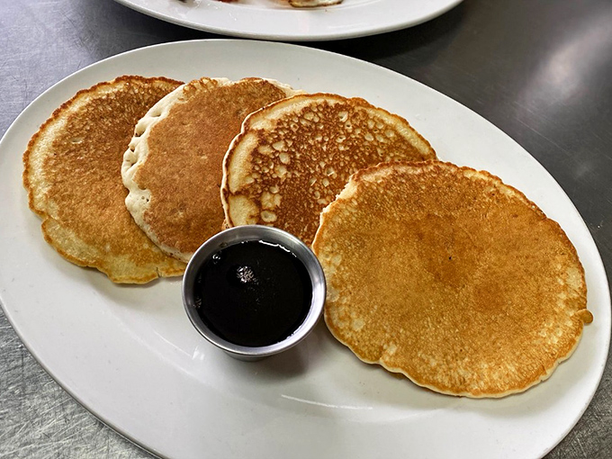 Pancakes so perfectly golden they look like they were painted by a Renaissance master. The syrup cup stands ready for the ceremonial pour.