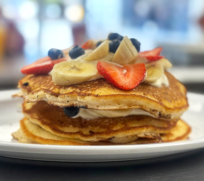 Pancakes stacked higher than your weekend expectations, crowned with fresh fruit that somehow makes you feel virtuous about ordering dessert for breakfast.