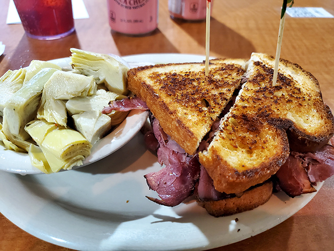 The pastrami sandwich arrives like a meaty monument, flanked by artichoke hearts&mdash;a reminder that sometimes the simplest pleasures are the most profound.