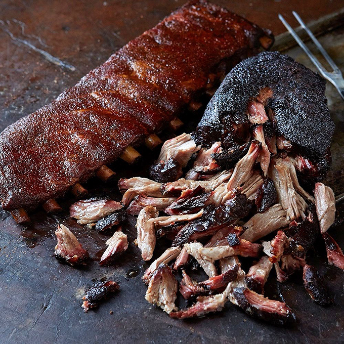The pork ribs and pulled pork share a cutting board like old friends, their bark-crusted edges and tender interiors telling tales of patient smoking.
