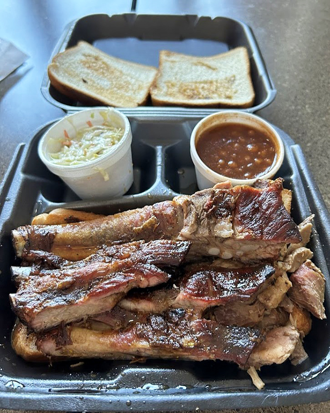 The holy trinity of Southern comfort: slaw, beans, and ribs arranged on a tray like edible artwork from the barbecue gods.