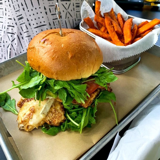 A burger masterpiece that demands your full attention &ndash; crisp arugula cascading over a perfectly seared patty, with sweet potato fries standing by for backup duty.