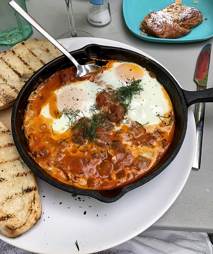 Shakshuka served in a sizzling skillet&mdash;eggs nestled in spiced tomato sauce with grilled bread standing by, ready for its supporting role in this Mediterranean masterpiece. 