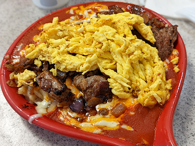A mountain of eggs atop seasoned steak on a fiery red plate. When breakfast decides to flex its muscles and show dinner who's boss.