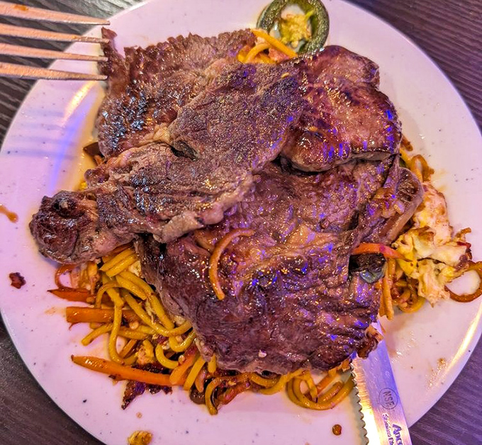 This isn't just steak&mdash;it's a meaty monument atop a mountain of noodles. The char marks tell stories of flame and patience that your taste buds need to hear.